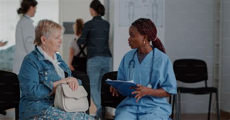 아프리카계 미국인 간호사가 시설 대기실에서 노인 여성에게 진단을 설명하고 있다 의료 보조원과 병을 앓고 있는 환자가 의료 치료와 회복에 대해 이야기합니다 사진