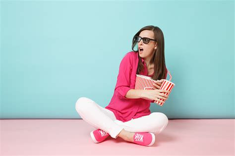 장미 셔츠 밝은 분홍색 파란 파스텔 벽 배경 스튜디오에 고립 된 영화 필름을 보고 바닥에 앉아 흰색 바지에 전체 길이 초상화 재미 있는 여자 패션 라이프 스타일 개념입니다