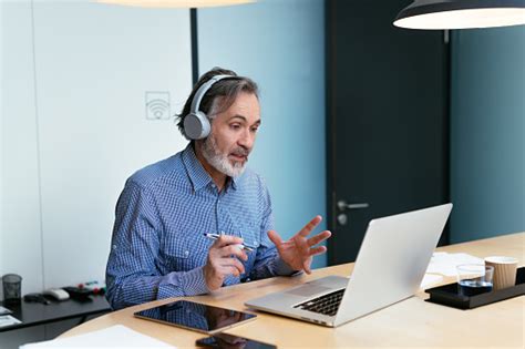 회색 머리 선임 사업가는 원격 동료와 화상 통화에 대해 이야기하고 사무실에서 웃고 있다 50 54세에 대한 스톡 사진 및 기타 이미지 50 54세 50 59세 결정