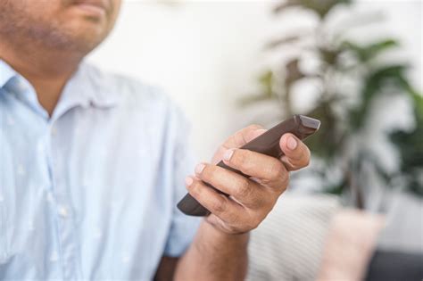 파란 셔츠를 입은 아시아 남자는 거실의 소파에 앉아 검은색 리모컨을 사용하여 Tv 채널을 변경합니다 휴일 휴식 신호 전송을 위한 적외선 기술 기술 휴식 광고에 대해 긍정적인