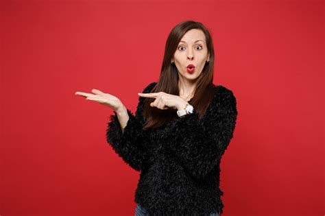 검은 모피 스웨터 포인팅 검지 손가락 손 옆으로 스튜디오에서 밝은 빨간 벽 배경에 고립에 충격된 젊은 여자의 초상화 사람들이