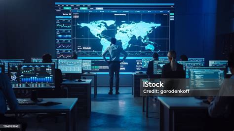 프로젝트 관리자는 신경망이 있는 큰 화면 옆에 서 있습니다 전문 컴퓨터 데이터 과학 엔지니어 팀이 어두운 시스템 제어 및 모니터링 통신 사무소에서 데스크톱에서 작업합니다