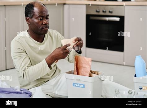 African Man Putting Papers In Container He Separating Garbage In The Kitchen For Recycling