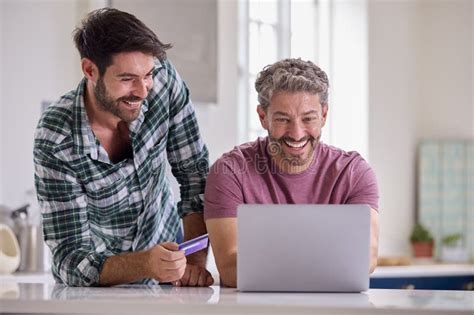 Same Sex Male Couple With Credit Card Using Laptop At Home To Book