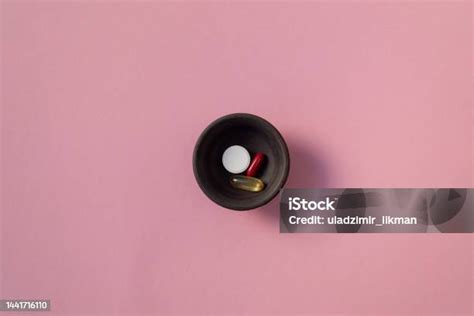 흰색 빨간색 및 노란색 비타민 알약은 텍스트를위한 공간이있는 분홍색 배경에 어두운 세라믹 그릇에 있습니다 의학과 건강 0명에