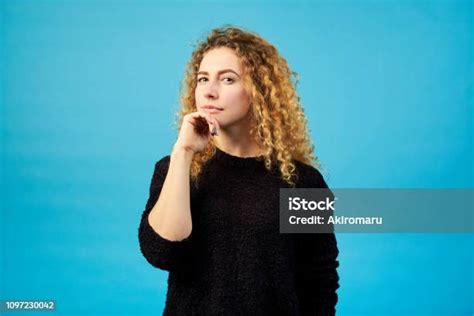 파란색 배경에 검은색 스웨터를 입고 카메라를 바라보는 생각 매력적인 빨간 머리 곱슬 소녀의 초상화 개념에 대한 스톡 사진 및 기타 이미지 Istock