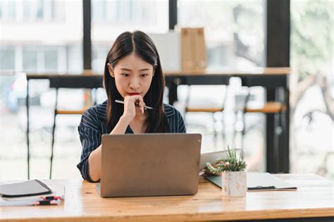 현대적인 사무실 환경에서 노트북으로 작업하는 집중적인 여성 펜을 들고 깊은 생각에 잠겨 있습니다 분위기는 차분하고 생산적이며 집중력과 창의성에 이상적입니다 20 24세에