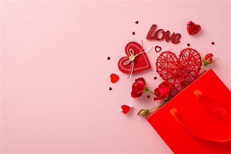 달콤한 사랑의 몸짓 파스텔 핑크 배경에 빨간 장미와 하트 모양의 색종이 조각으로 장식된 종이 봉지의 평면도 발렌타인 데이 선물로 적합하며 특별한 메시지를 위한 공간을