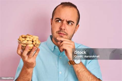 질문에 대해 생각 하는 고립 된 분홍색 배경 심각한 얼굴 위에 서 땅콩그릇을 들고 젊은 남자 매우 혼란 스러운 아이디어 개념에 대한 스톡 사진 및 기타 이미지 Istock