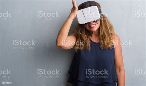 중세 스페인 여자 머리에 손으로 압박 하는 가상 현실 안경을 쓰고 회색 그런 지 벽에 서 수치심과 깜짝 얼굴로 충격 분노와 좌절 두려워 하 고 실수에 대 한 화가 3차원