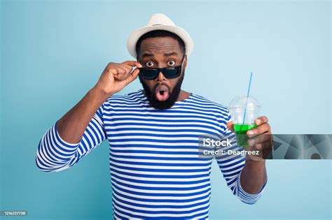 흥분 된 충격 어두운 피부 남자 여행자 보유 녹색 알코올 음료 컵 이륙 사양 참조 매력적인 여자 착용 흰색 태양 모자 줄무늬 선원 셔츠 고립 된 블루 컬러 배경 남자에 대한