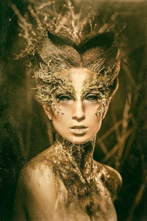 A Woman With Gold Paint On Her Face And Body Is Standing In Front Of Trees