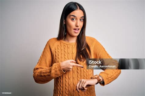 젊은 아름다운 갈색 머리 여자 를 입고 캐주얼 스웨터 위에 고립 된 흰색 배경 에 서둘러 가리키는 시계 시간 조바심 화가 와 화가 마감 지연 가리키기에 대한 스톡 사진 및
