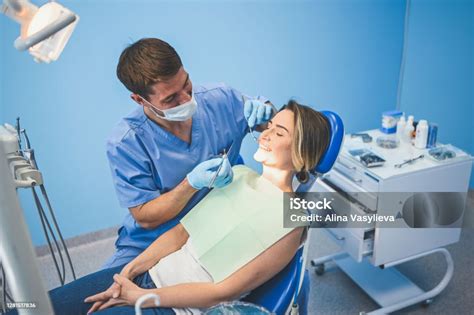 치과 의사는 치과 사무실에서 치과 장비를 사용하여 환자의 치아를 검사합니다 스토마토로지와 건강 개념 일회용 의료 용 안면 마스크를 쓴 젊은 잘생긴 남성 의사 행복한 여자 2