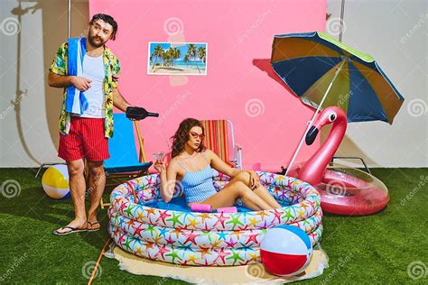 Man Wearing Tropical Shirt And Red Shorts Pours Drink While Woman