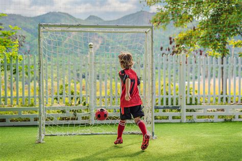 빨간 축구 유니폼을 입은 귀여운 소년이 야외에서 축구 축구를 하고 있다 아이들이나 아빠와 함께 스포츠를 하는 활동적인 아이 여름에 즐거운 미소를 짓는 행복한 소년 6 7