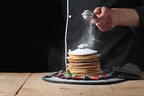 가루 설탕과 딸기의 봉사 팬케이크 요리사 여자 핸드입니다 아름 다운 음식 아직도 인생입니다 이미지 약간 톤된 어두운 검은 배경에 텍스트 영역 가로 보기 Shrove