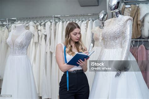 웨딩 부티크에서 신부 복장 근처에서 포즈를 취하는 일기와 펜을 가진 여성 드레스 메이커 Bridal Show에 대한 스톡 사진 및 기타 이미지 Bridal Show