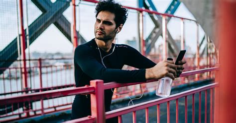 핸드폰 장치를 손에 들고 오디오 북의 줄거리를 숙고하는 잠겨있는 유럽 주자 전자 헤드폰 및 모바일 앱을 통해 음악 재생 목록을 듣는 사려 깊은 운동 보디 빌더 30 34세에