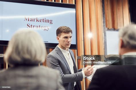 컨퍼런스에서 마케팅 전략에 대해 말하면서 통계 논문을 가리키는 회색 정장의 심각한 잘 생긴 젊은 Smm 전문가 연설에 대한 스톡
