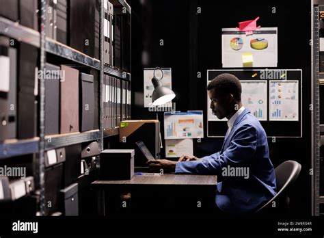 African American Police Officer Analyzing Investigation Files Working Overtime At Confidential