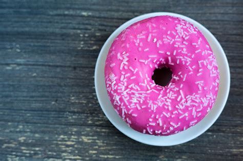 하얀 둥근 접시와 오래된 나무 회색 배경에 밝은 분홍색 도넛을 올려 놓으십시오 격리된 개체가 닫힙니다 아침 식사로 전통적인 미국 과자 복사 공간 위에 흰 설탕 장식입니다 0