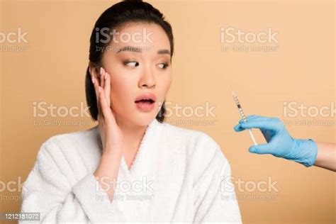 베이지 색 배경에 아름다움 주입주사기와 미용사 손 근처 목욕 가운에 무서운 아름다운 아시아 여자 2명에 대한 스톡 사진 및 기타 이미지 Istock