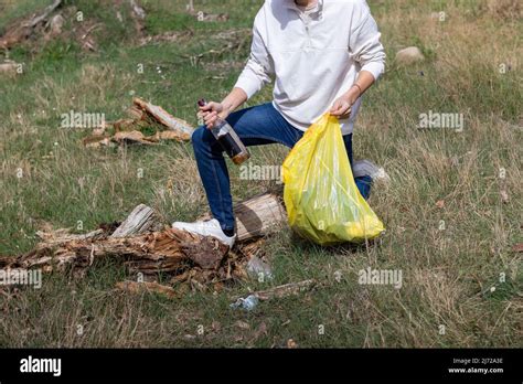 Unrecognizable Man Crouching Down Picking Up Bottle Of Alcohol After A Music Festival Party