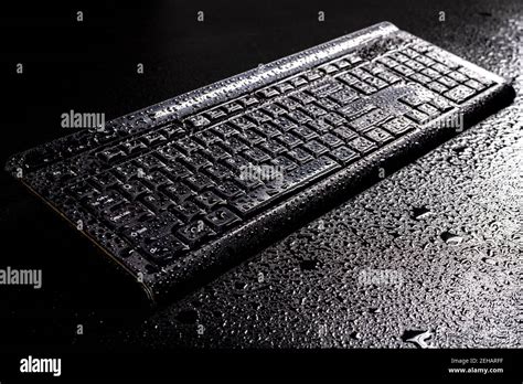 Wet keyboard from a personal computer. Water drops on an electronic device. Dark background ...