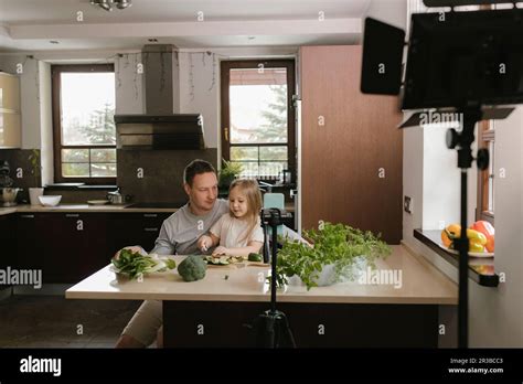 Father And Daughter Cutting Vegetable Filming Tutorial At Home Stock