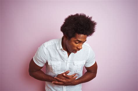 소화 불량 고통스러운 질병 이 좋지 않은 느낌 때문에 위에 손으로 고립 된 분홍색 배경 위에 서 있는 흰색 셔츠를 입고 있는 젊은 미국 남자 아쉬 컨셉 건강관리와 의술에