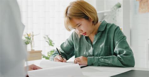 젊은 아시아 소녀 여성 환자가 의료 양식 또는 서명 건강 보험 계약에 서명하고 건강 병원 사무실의 책상에 앉아 있는 흰색 의료 유니폼을 입은 여성 의사와 클리닉에서 회의에