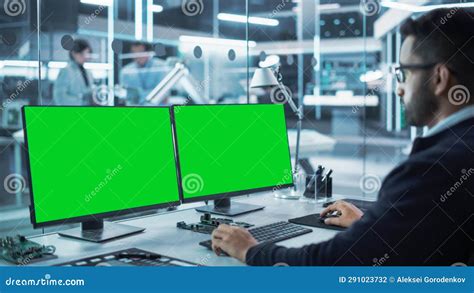 Software Developer Working On A Desktop Computer With Two Green Screen Chromakey Display Screens