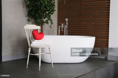 콘크리트 벽 나무 칸막이 및 흰색 욕조가있는 현대적인 욕실 인테리어 디자인 수건과 하트가 있는 빈티지 의자 발렌타인 데이 개념 휴식 마사지 선물 관리 휴식 하트 모양에 대한