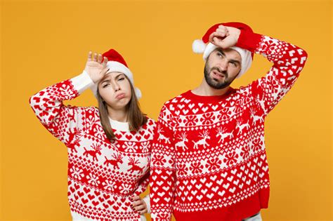 피곤한 젊은 산타 커플 친구 남자 여자 빨간 스웨터 크리스마스 모자를 입고 노란색 배경 스튜디오 초상화에 고립 된 머리에 손을 넣어 새해 축하 메리 홀리데이 컨셉 2명에