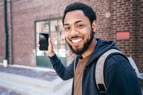 Un Chico Guapo Sonriendo Y Mostrando Su Celular A La Cámara Foto Premium