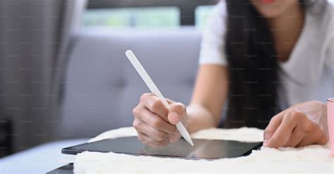 소파에 앉아 디지털 태블릿에 스타일러스 펜을 들고 웃고 있는 젊은 여성의 자른 사진 사진 Unsplash의 통신 이미지