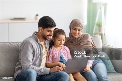 젊은 무슬림 부모와 함께 노트북을 사용 하 여 소녀 인터넷 서핑 또는 누군가와 화상 채팅 소파에 앉아 3 명에 대한 스톡 사진 및 기타 이미지 Istock