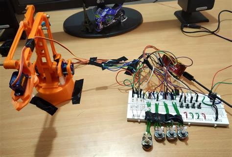 An Orange Robot Sitting On Top Of A Wooden Table Next To A Keyboard And Wires