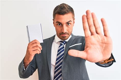 진지하고 자신감있는 표정 방어 제스처로 정지 표지판을 하는 오픈 핸드로 고립 된 배경 위에 빈 노트북을 들고있는 젊은 잘 생긴 사업가 경계 표지에 대한 스톡 사진 및 기타