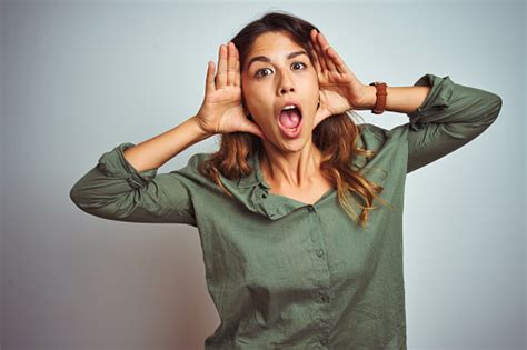 회색 고립 된 배경 에 서 녹색 셔츠를 입고 젊은 아름다운 여자는 얼굴을 보여주는 손으로 우우를 들여다 쾌활한 재생 미소 놀랍고