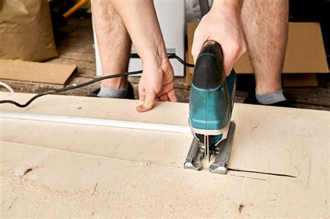 합판에서 전기 퍼즐로 부품을 톱질하고 절단하는 건설 노동자의 남성 손 절단 프로세스입니다 프렛소와 인테리어 장식의 Diy 건물