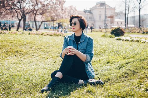 공원에 앉아 휴식을 취하는 아름 다운 여자 가 서 커피를 마시는 매력적인 갈색 머리의 초상화 따뜻한 봄 날 야외에서 즐기는 현대 소식통 세련 된 소녀 스트리트 스타일