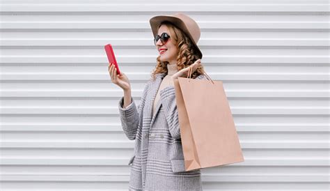 흰색 배경에 코트 둥근 모자를 쓰고 쇼핑 백으로 스마트 폰으로 셀카를 찍는 행복한 미소 젊은 여성의 초상화 25 29세에 대한 스톡 사진 및 기타 이미지 Istock