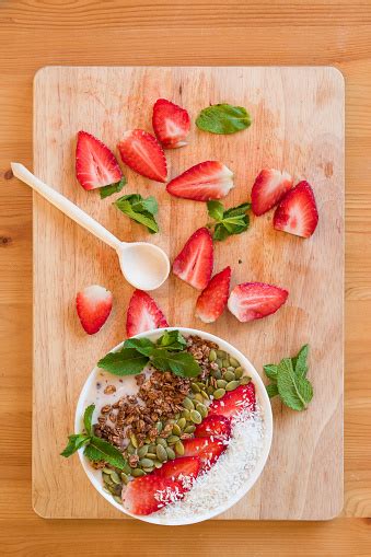 아침 베리 스무디 그릇은 딸기 호박 씨앗 코코넛 Muesli 신선한 민트 얹은 딸기 바나나 스무디 그릇입니다 건강 한 아침 식사 또는 간식 나무 식기입니다 그래놀라에 대한