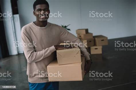 젊은 아프리카계 미국인 남자가 상자를 들고와 새로운 사무실에 재배치 하는 동안 카메라에 웃 고 경영자에 대한 스톡 사진 및 기타 이미지 Istock