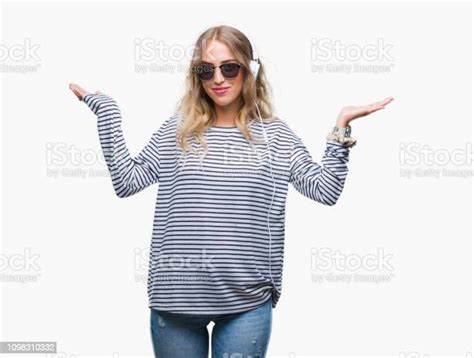 아름 다운 젊은 금발 여자 팔과 손을 제기와 격리 된 배경 우 둔 하 고 혼란 스 러 워 식 이상의 헤드폰과 선글라스 입고 의심