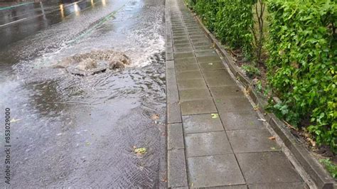 Water Lifting An Iron Sewage Manhole Cover On The Road Strong Water Pressure Flowing Onto The