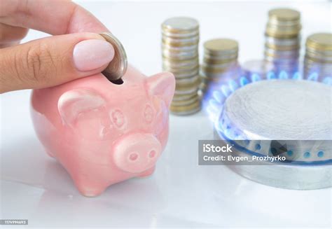 부엌에서 가스 난로의 불꽃 근처 동전과 돼지 저금통 여성 손 비용 에너지 효율 및 가정에서 천연 가스를 절약의 상징적 인 이미지 연료 및 전력 생산에 대한 스톡 사진 및