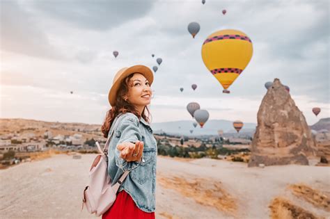 터키 카파도키아에서 젊은 여성이 열기구를 배경으로 치솟는 자신감 넘치는 팔로우 미 포즈를 취하는 모험에 참여하세요 열기구에 대한 스톡 사진 및 기타 이미지 Istock